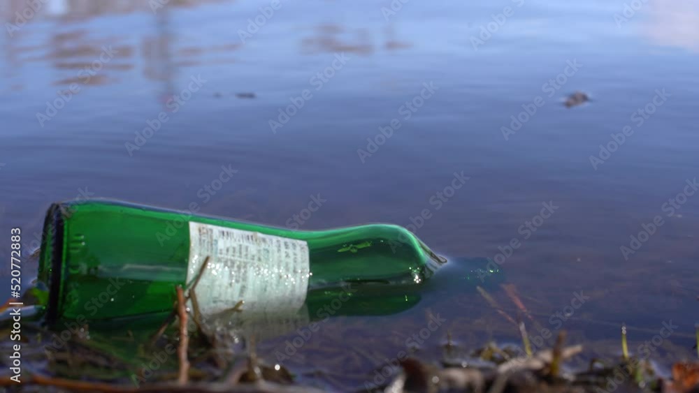Water pollution, glass bottle in water. One hand takes the glass bottle ...