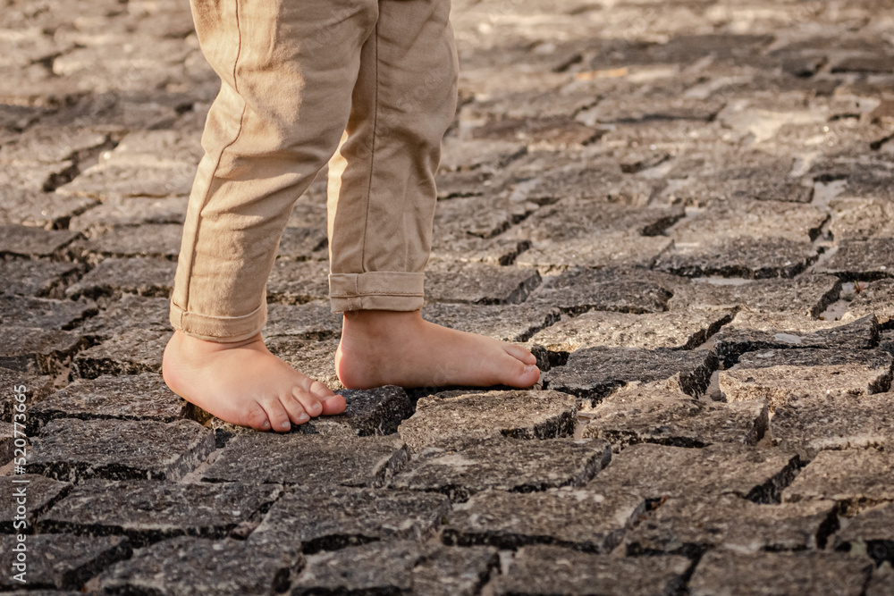 Bare children's feet on the cobblestones. The child is barefoot ...