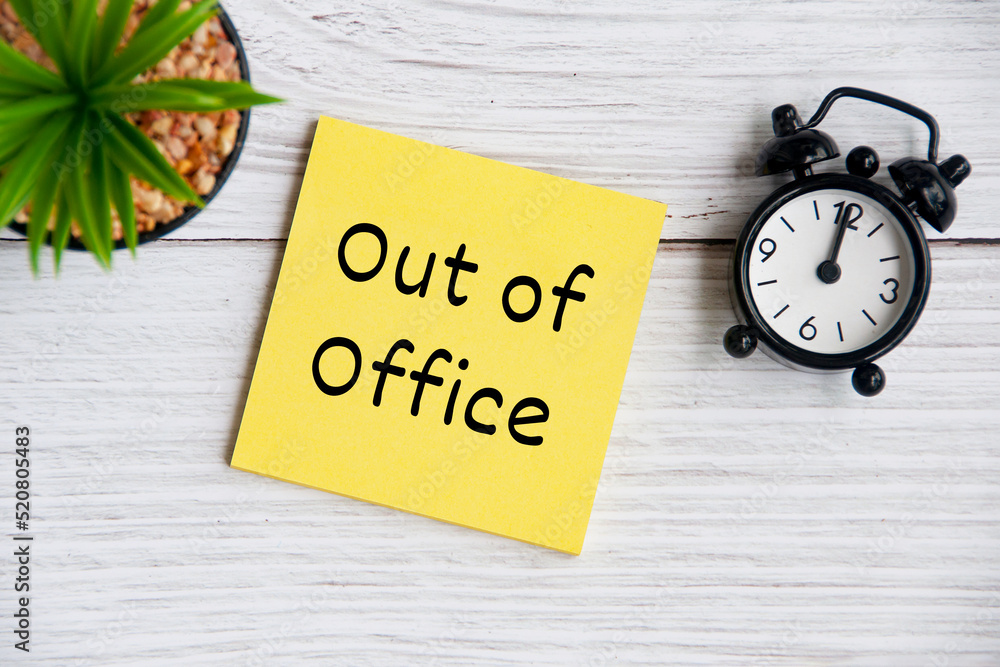 Out of office text on sticky note with alarm clock and plant background ...