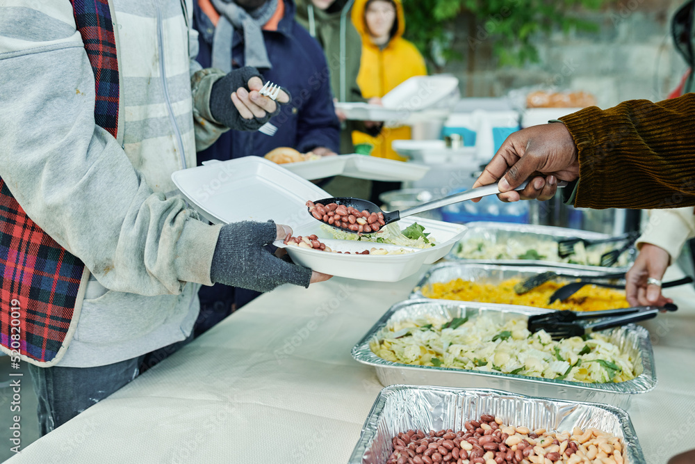 Close-up of volunteers serving homeless people and putting meal on ...