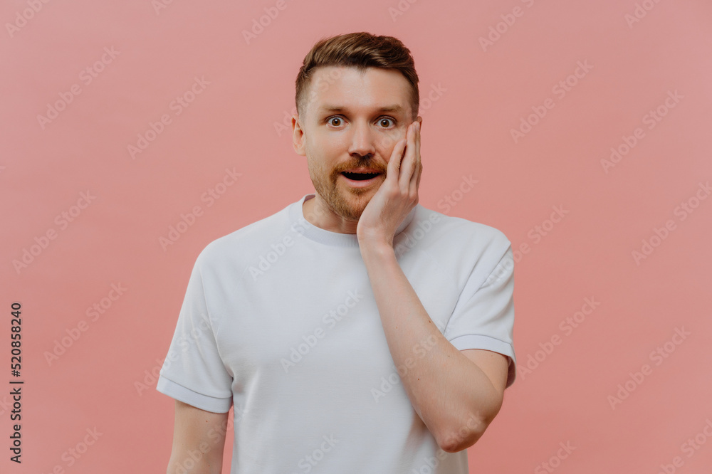 Amazed bearded man keeps hand on cheek stands speechless cannot believe ...