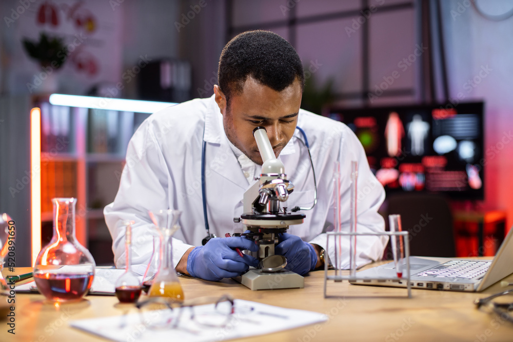 Young african american male researcher looking at the microscope ...