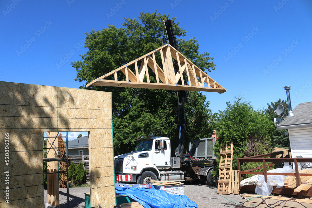 Truck lifting roof trusses with truck-mounted crane, high in the air on ...