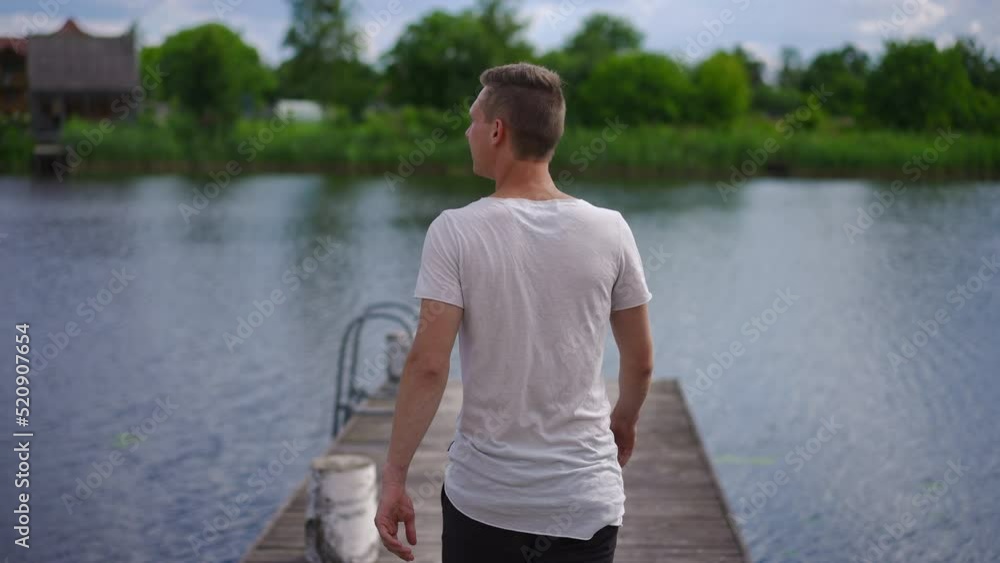 Back view confident young Caucasian man walking in slow motion to river ...