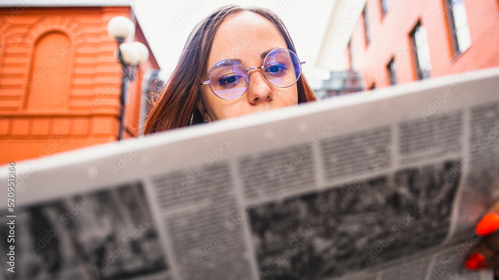Thoughtful young woman reading newspaper on street. Confused young ...