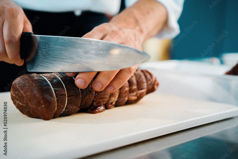Professional restaurant kitchen, close-up: Chef cut meat for filet ...