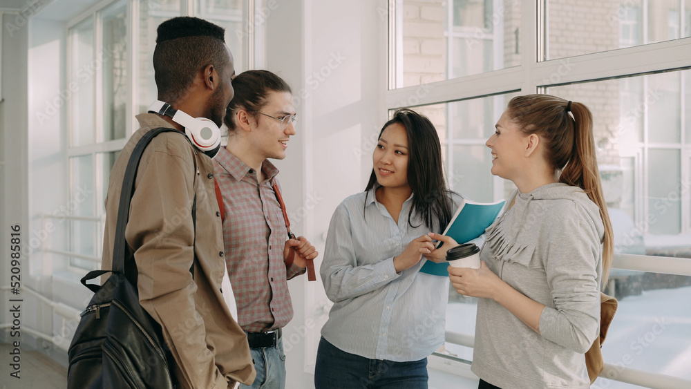 Four multi-ethnic studens are standing in big white glassy spacious ...