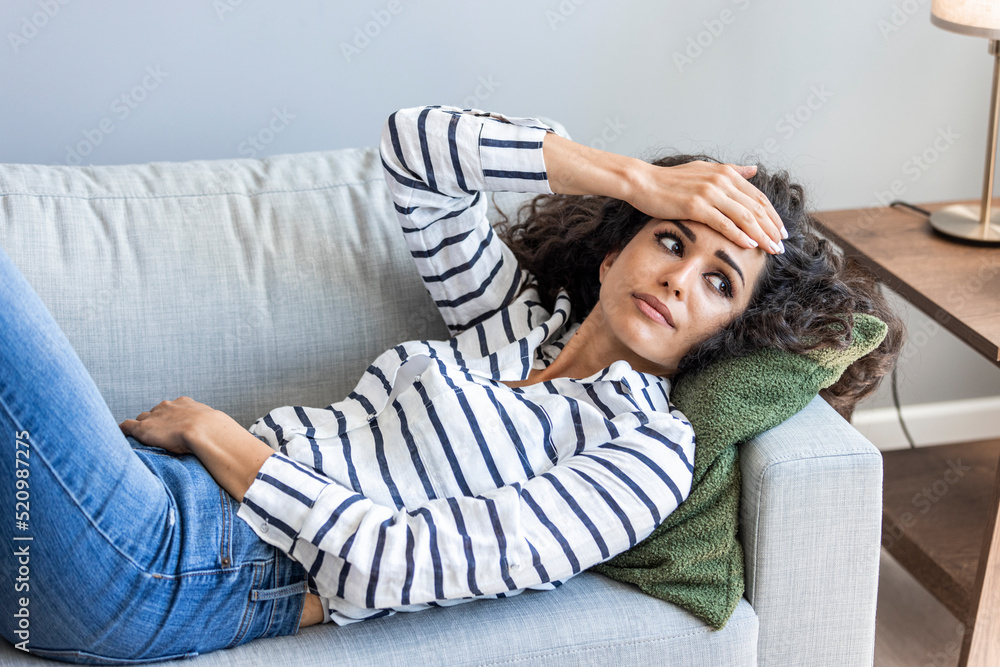 Upset depressed young woman lying on couch feeling strong headache ...