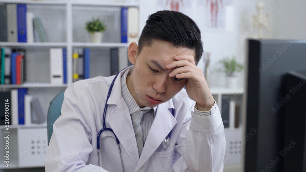 asian doctor experiencing stress at work is propping head and touching ...