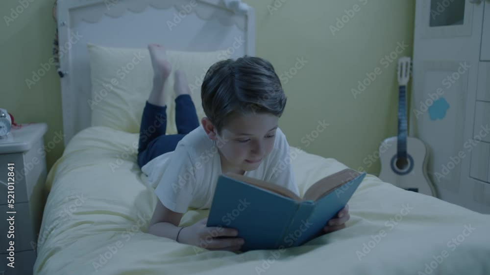 Little boy reading a book on the bed in the bedroom at night. Children ...