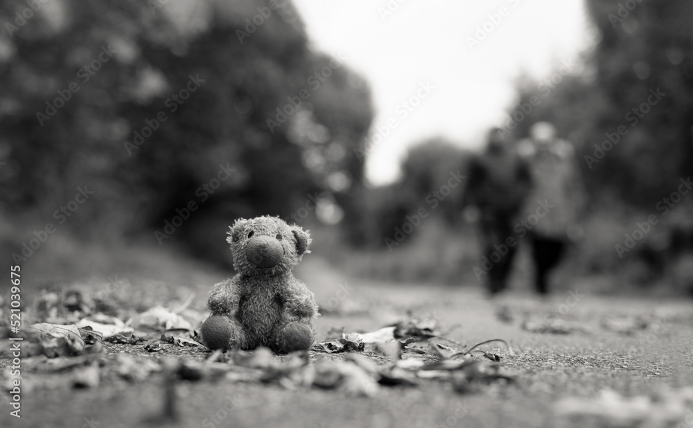 Lost Teddy bear with sad face sitting on footpath with blurry people ...