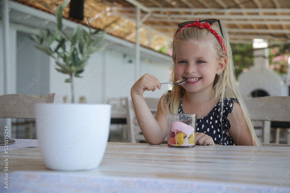 Happy little girl eating tasty fresh ice cream in cafe. Adorable little ...