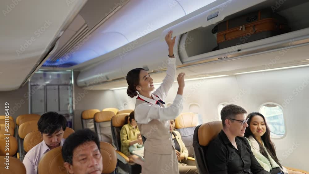 Asian woman flight attendant walking on airplane aisle closing luggage ...