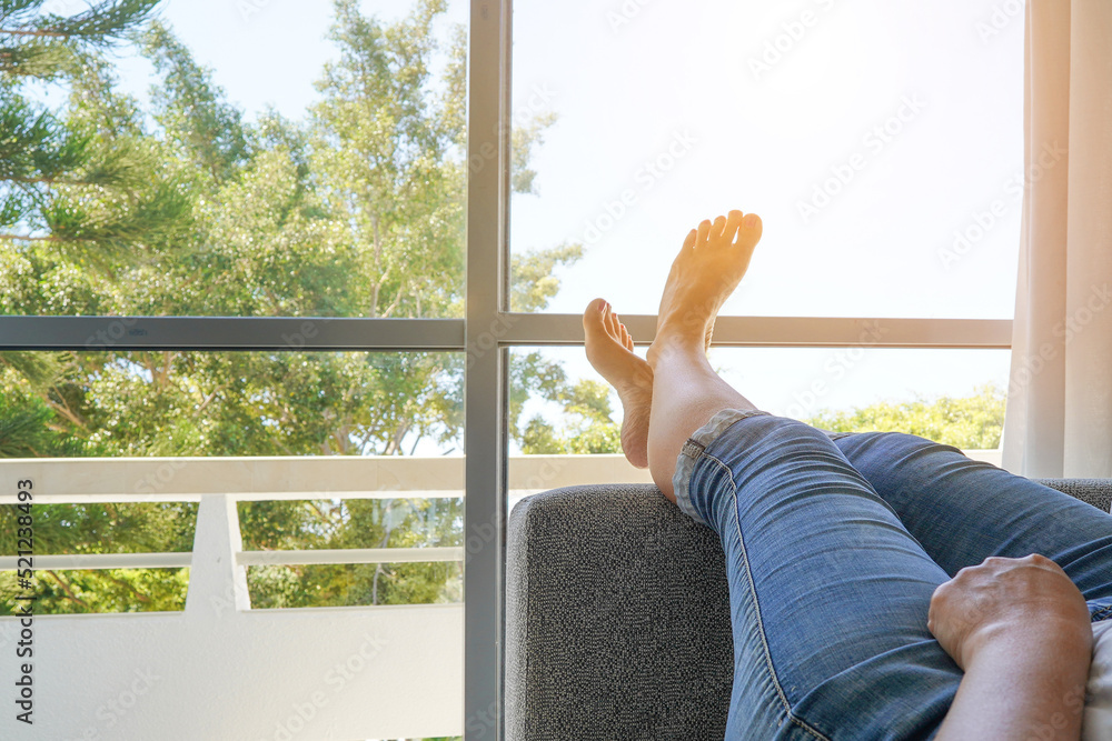Women legs on the sofa couch. Woman feet up against window. Young woman ...