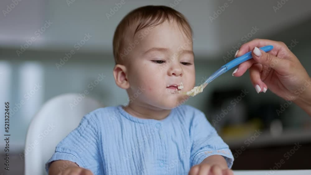 Feeding a little kid from a spoon. Mom's hand shoves a full spoon to ...