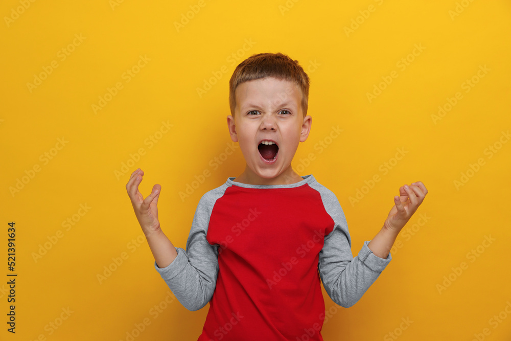 Angry little boy screaming on yellow background. Aggressive behavior ...