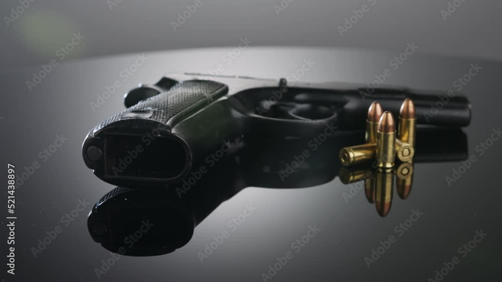 Gun Control. 9mm handgun with bullets rotating on a reflective surface ...