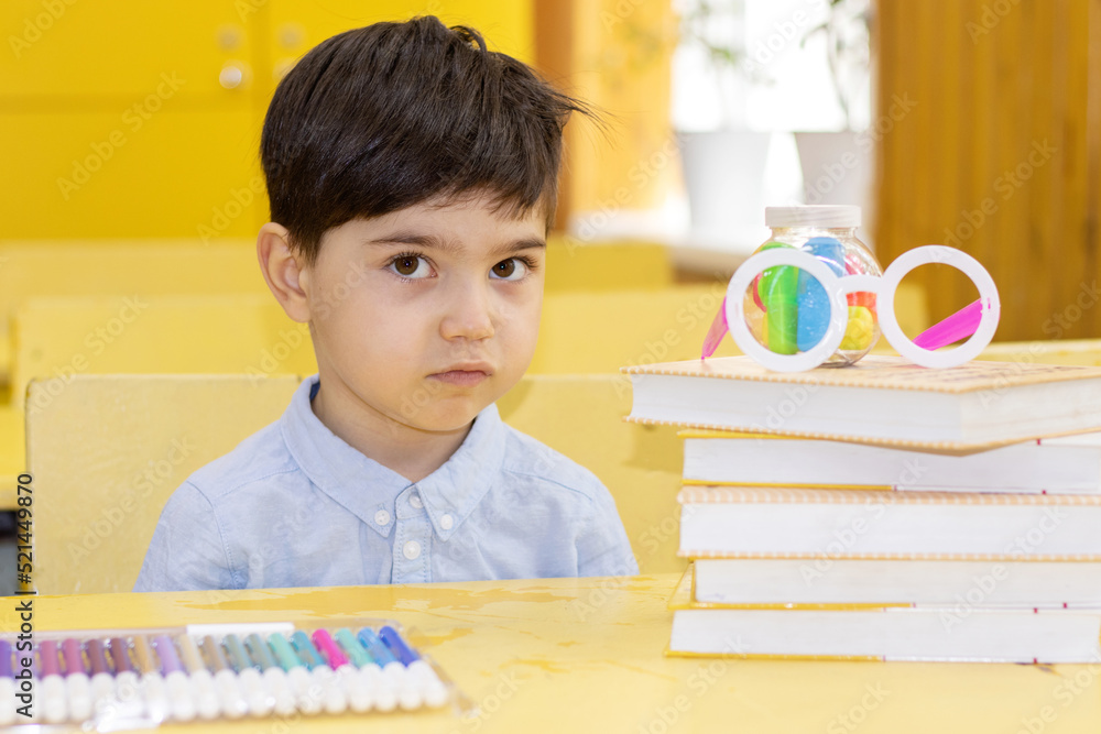 upset unhappy preschool kid sitting in school desk with serious face ...
