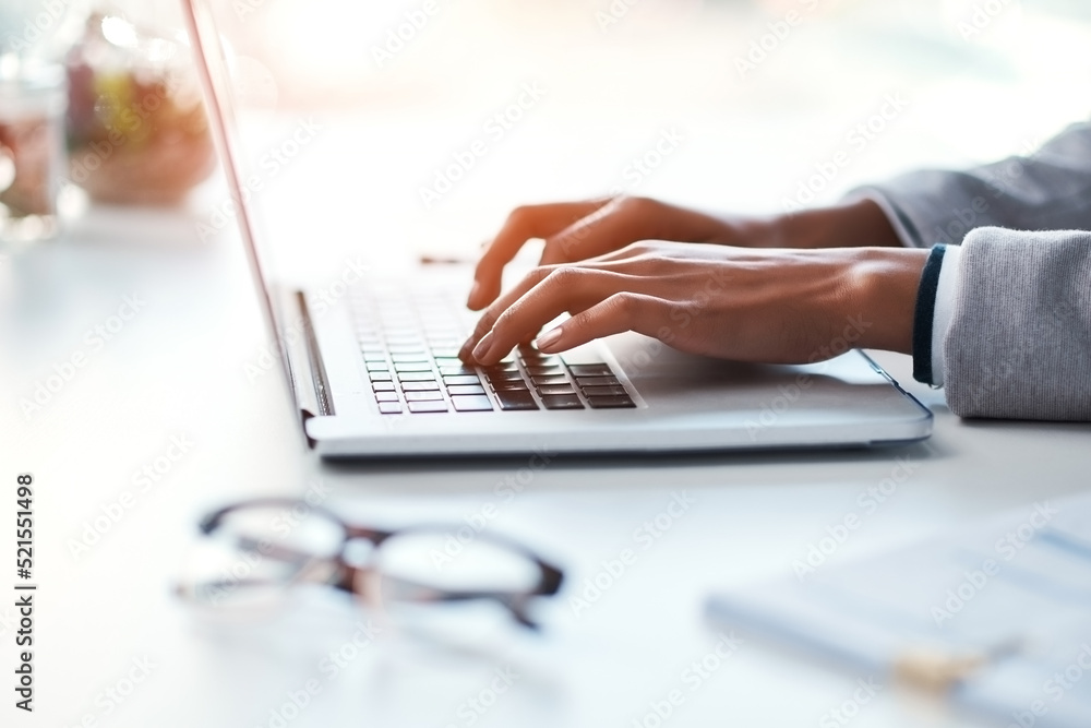 Businesswoman typing work on a laptop at her desk in a modern office ...