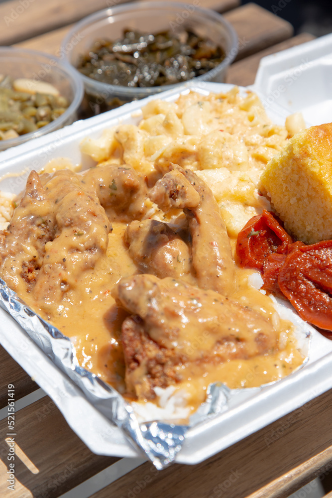 A view of a styrofoam container of soul food, featuring smothered ...