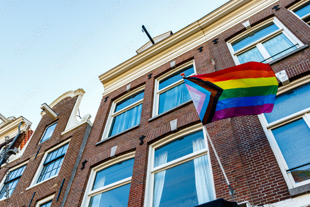 Old Dutch canal houses in Amsterdam with a Progress Pride Flag on their ...