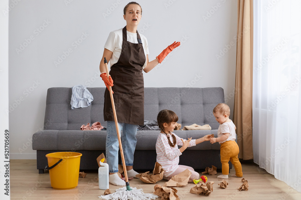 Portrait of tired mother wearing brown apron cleaning at home, woman ...