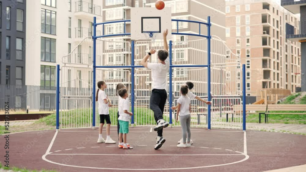 Coach throwing basketball in basketball hoop on court. Children play a ...