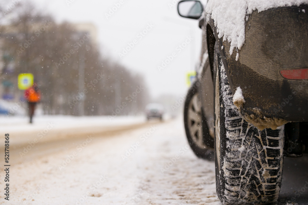 Rear view of a snow-covered car with studded tires on the background of ...