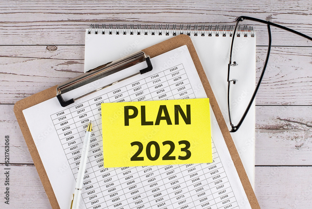 PLAN 2023 text on yellow sticky on clipboard with chart, wooden ...