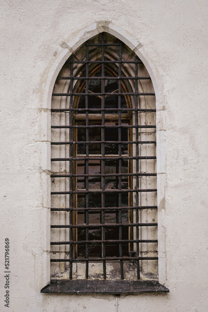 Old white stone wall with one arched grating window on the street ...