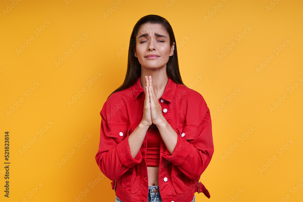 Beautiful woman holding hands clasped and eyes closed while standing ...