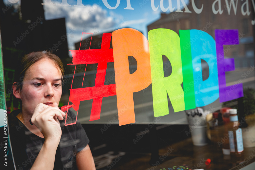 Girl decorating a shop window with a Gay Pride sign supprting diversity ...