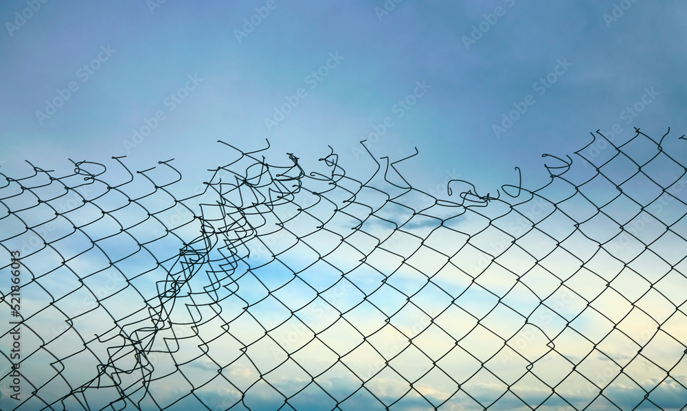 Opening in metallic fence against a blue sky with white clouds ...