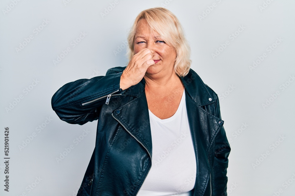 Middle age blonde woman wearing leather jacket smelling something ...