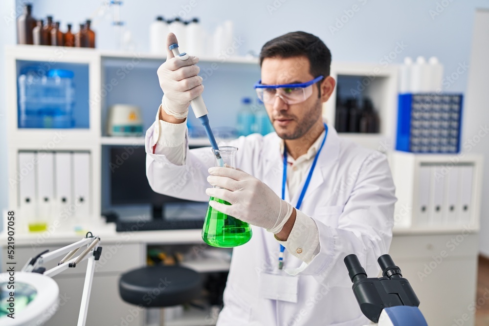 Young hispanic man scientist measuring liquid using pipette at ...