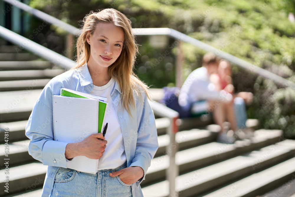 Pretty girl university student holding notebooks looking at camera posing for outdoor portrait ...