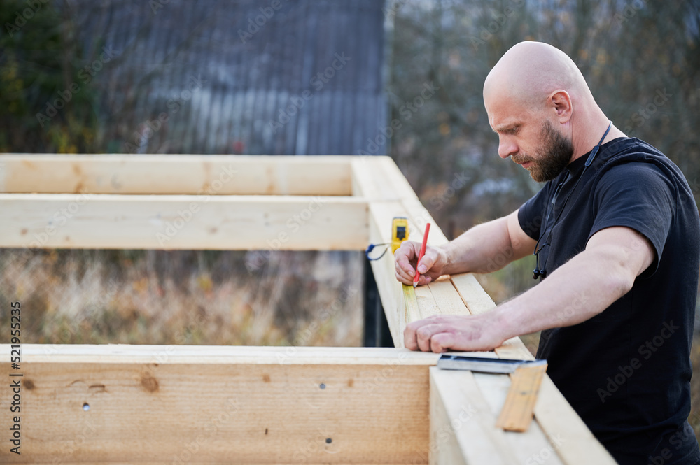 Man worker building wooden frame house on pile foundation. Bald ...