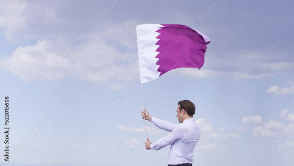 Young man waving the Qatari flag. The Qatari flag flutters in the wind ...