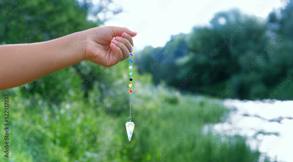 Hand holding dowsing pendant against abstract green natural background ...