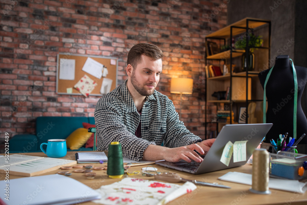A handsome man with a bushy beard is working on designing clothes as he ...