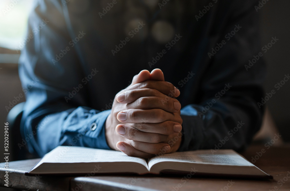 Foto de man sitting and praying to god with his hands on the open bible ...