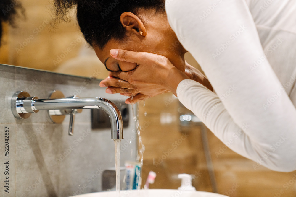 Adult african woman washing her face in bathroom close-up Stock Photo ...