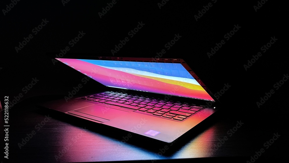 Laptop with half lid open on a table lit with colorful desktop screen ...