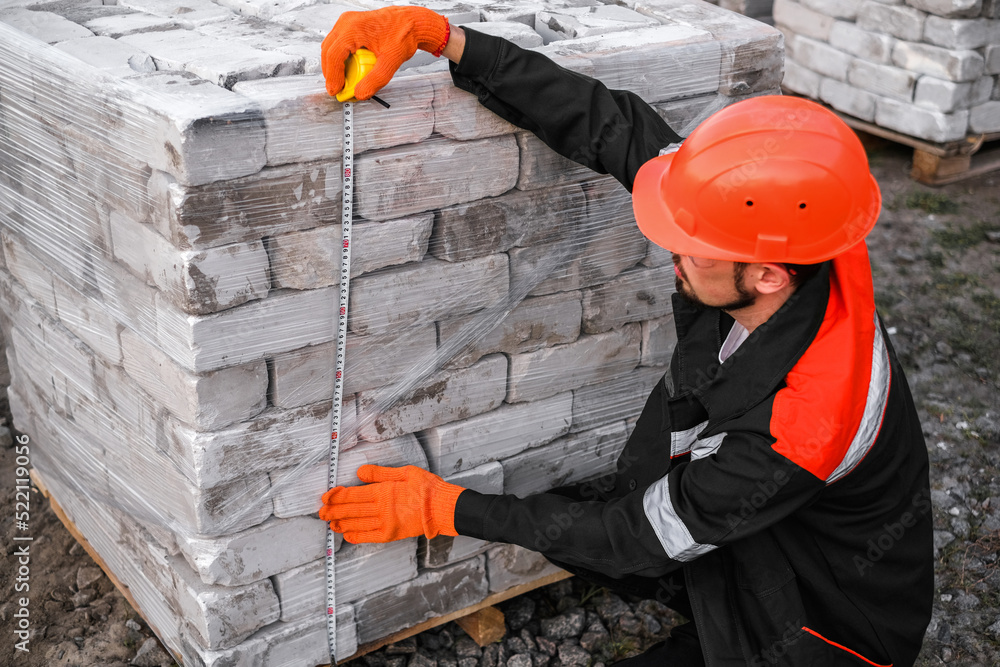 male builder measures the size of brick pallets at a construction site ...