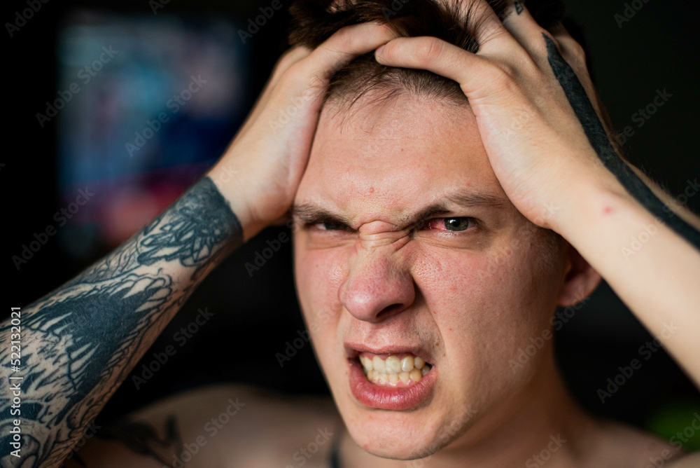 portrait of a young guy with a tattoo gritting his teeth and holding ...