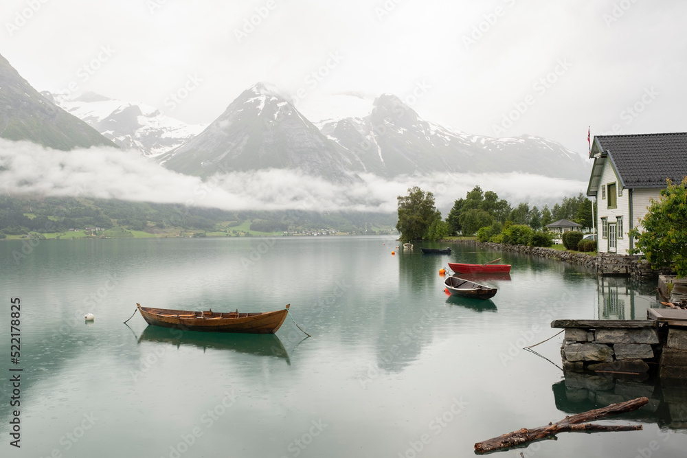A bucolic image with moored wooden boats, a dock, o house and mountain ...