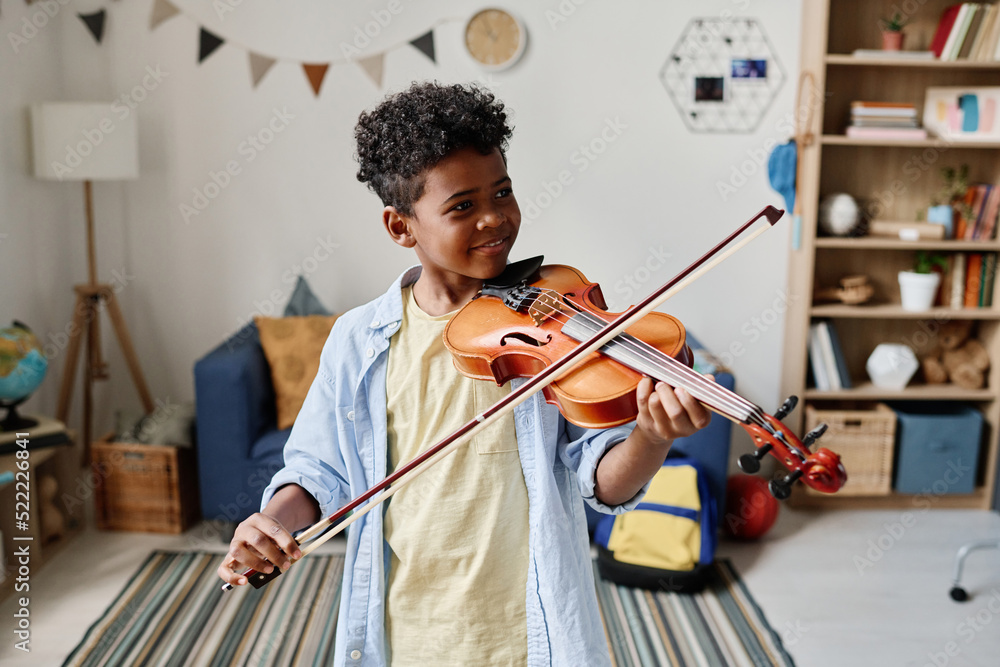 Foto de African boy playing violin during lesson while standing in his ...