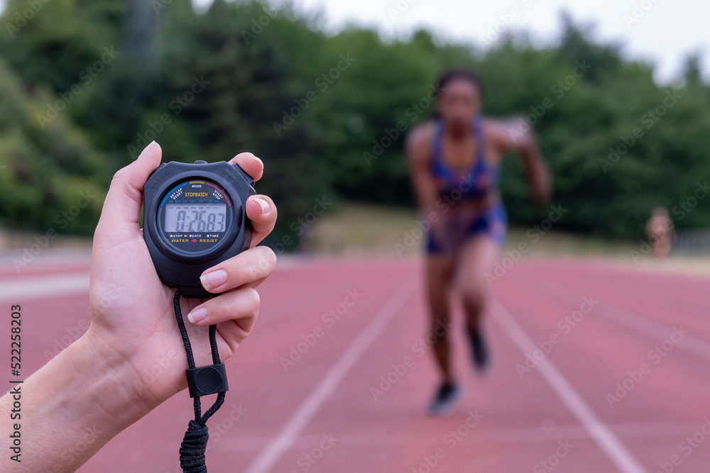 Female athlete running on running track, hand with stopwatch in ...