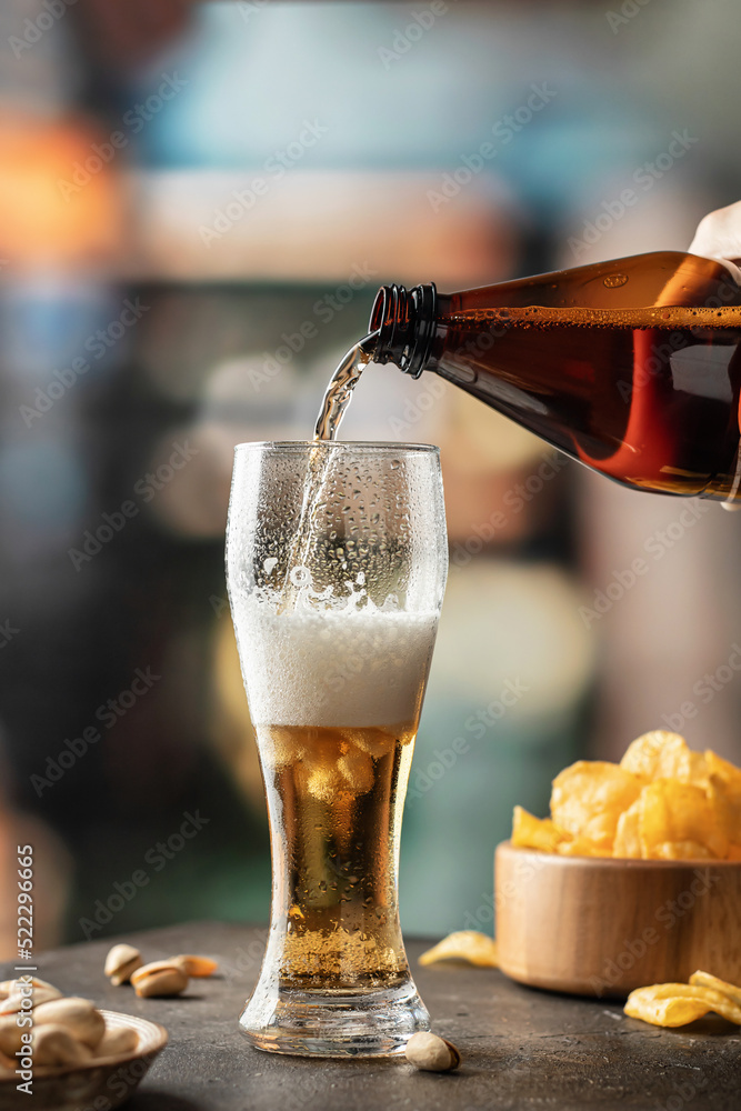 Pouring light foamy beer into glass in bar background. Traditional ...