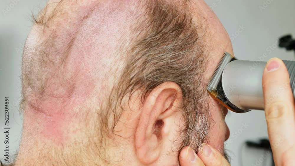 Man shaves his head. Amateur haircut in the bathroom. An overgrown man ...